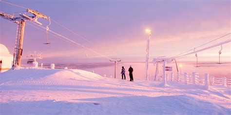 2 명의 스키어가 산 꼭대기에 서 있습니다 스키 슬로프 위에 밝고 화려한 일출 스키 리프트 등이 있습니다 쿠 사 모ruka 핀란드 라플란드 스키 리조트 2명에 대한 스톡