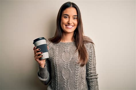 젊은 아름다운 갈색 머리 여자 마시는 유리 의 커피 위에 고립 된 흰색 배경 와 행복한 얼굴 서서 치아를 보여주는 자신감 미소와 미소 보기 정적 활동에 대한 스톡 사진 및