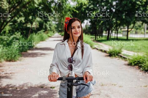 귀여운 갈색 머리 소녀는 그녀가 흰색 셔츠를 입고공원에서 전기 스쿠터를 타고 에코 운송 및 임대료의 개념 거리에 대한 스톡 사진 및 기타 이미지 Istock