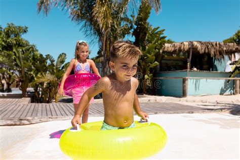Happy Biracial Brother And Sister Holding Swim Rings By The Swimming