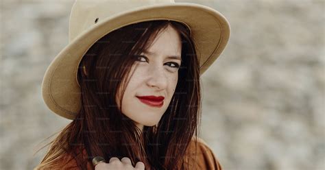 모자 가죽 가방 프린지 판초와 부츠를 가진 아름다운 세련된 힙스터 보헤미안 여자 집시 히피의 소녀는 산의 강 바위 근처에서