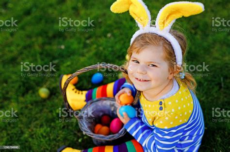 녹색 잔디에 앉아 토끼 귀를 착용 귀여운 어린 유아 소녀는 따뜻한 화창한 날 야외에서 전통적인 부활절 색달걀 사냥과 재미를 가족 휴가를 축하하는 행복한 아이 2 3 살에