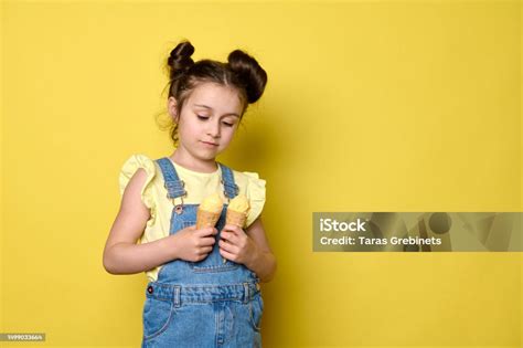 파란색 데님 작업복을 입은 귀여운 아기 소녀 맛있는 아이스크림 한 스쿱과 함께 와플 콘을 들고 노란색 배경에 고립되어 있다 6 7 살에 대한 스톡 사진 및 기타 이미지