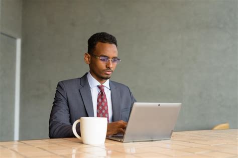 African Businessman Wearing Suit And Tie In Coffee Shop While Using