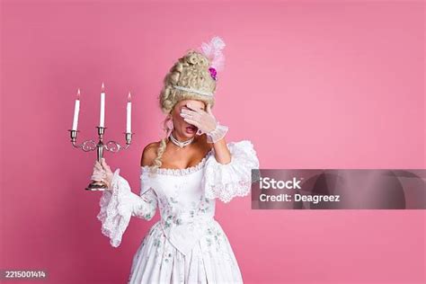 우아한 바로크 양식의 복장을 입고 왕족과 현대적인 활기가 조화를 이루는 분홍색 배경에 촛불을 들고 있는 매력적인 젊은 여성입니다 40 44세에 대한 스톡 사진 및 기타