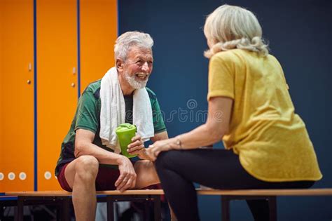 Sporty Mature Man And Woman In Gym Locker Room Sitting Facing Each