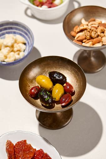 올리브의 이탈리아 전채 요리는 향신료와 향신료를 섞습니다 그림자가있는 흰색 테이블 위의 금속 그릇에 절인 올리브 녹색과 검은 색 올리브가있는 미적 구성 토스카나에서 점심