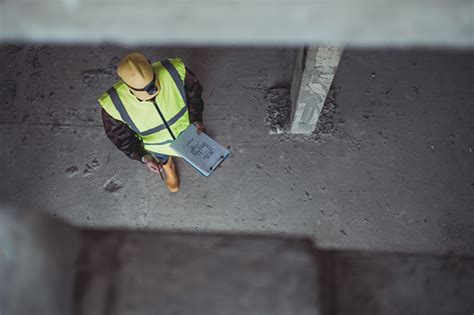 건설 현장에서 설계자 독서 계획의 초상화 안전 조끼를 입은 안전 헬멧을 착용한 토목 엔지니어가 디지털 태블릿을 사용합니다 적응