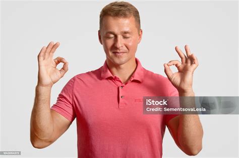 매력적인 젊은 남자의 사진 괜찮아 제스처를 만드는 눈을 감고 흰색 바탕에 분홍색 티셔츠를 입은 그의 승인 포즈를 보여줍니다 사람 신체 언어와 몸짓 개념 감정에 대한 스톡