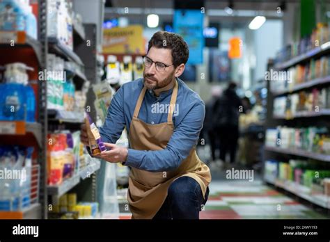 Store Employee Kneeling In Supermarket Aisle Arranging Products Man