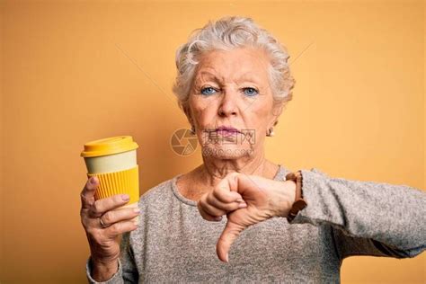 高贵的美女喝咖啡站在孤立的黄色背景上面脸发怒负表情示不喜欢用拇指往下冲拒绝概高清图片下载 正版图片504639446 摄图网