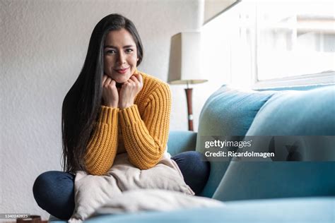 Latin Woman Is Sitting On The Sofa In Her Living Room Looking At The