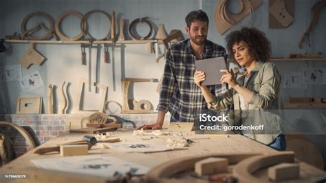 태블릿 컴퓨터를 사용하고 가구 워크샵에서 새로운 나무 의자 디자인을 논의하는 재능있는 두 명의 중소 기업 소유자 목수와 로프트 스튜디오에서 일하는 젊은 여성 견습생 2명에