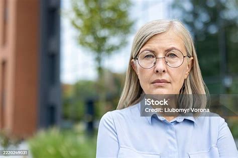 A Sophisticated Mature Woman With Glasses Poses Outside A Modern