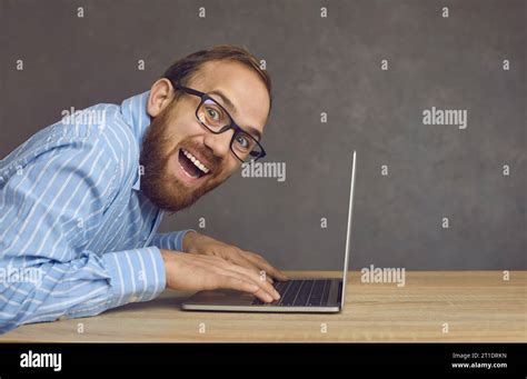 Side View Portrait Of A Joyful Crazy Hacker Or Programmer Sitting At A Table Typing On A Laptop