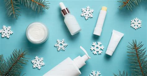 파란색 배경에 겨울 스킨케어 화장품 세트 포장 디자인 템플릿입니다 모이스처 라이저 크림 병 립스틱 펌프 병 튜브 눈송이 및 전나무 나뭇 가지 플랫 레이 평면도