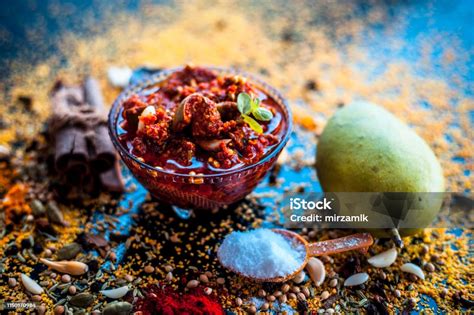 인기 있는 인도 파랑 유리 그릇에 있는 망고의 채소 절 임 즉 유리 그릇 이나 케리 카 Achar에 향신료와 망고를 포함 한 전체 원료와 함께 검은 색 빛나는 표면에 강황에