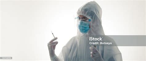 외과 용 얼굴 마스크와 얼굴 방패를 착용하고 있는 헤이즈마트 양복을 입은 아시아 여성 의사는 코로나바이러스 치료를 위한 백신을