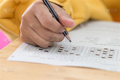 高中生或大学生手拿试卷，在答题纸上写试卷，标准化考试光学形式放在桌上，在教室里做期末考试。教育素养的