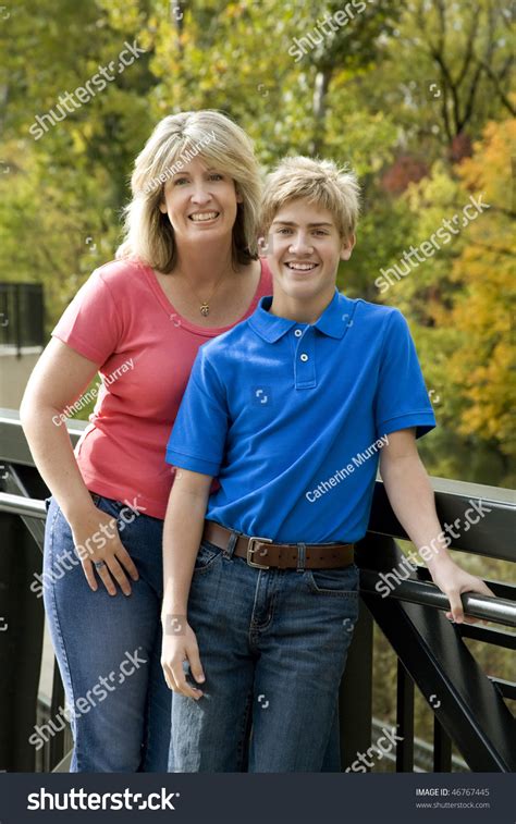 A Blond Mom And Teenage Son Posing Near A Line Of Trees Stock Photo