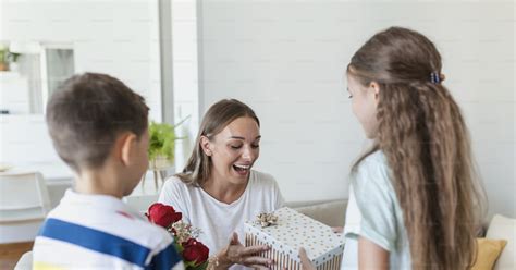 어머니에게 꽃을 선물하는 행복한 아이들 해피 어머니의 날 어린이 소년과 소녀는 웃는 어머니를 축하하고 휴일 축하 기간 동안 장미 꽃다발과 선물 상자를 제공합니다 사진