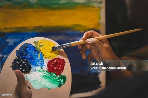 암실에 있는 아시아의 남자는 따뜻한 조명 예술가가 붓과 다양한 아크릴 색으로 그림을 그리는 작업을 하고 있다 예술 개념으로 크리에이티브 스튜디오에서 캔버스에 있는 남자