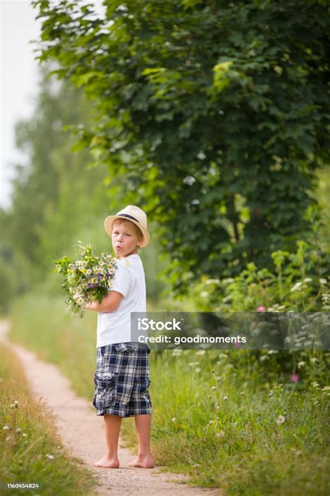시골 길에 서서 야생 꽃의 무리를 들고 밀짚 모자에 귀여운 맨발 아이 소년의 초상화 공원에서 걷는 아이 야외 행복한 여름과 라이프 스타일 개념 어린 시절 8월에 대한 스톡