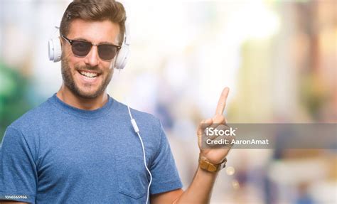 잘생긴 젊은이 얼굴에 큰 미소와 함께 고립 된 배경에 음악을 듣고 하는 헤드폰을 착용 측면 카메라 보고 손과 손가락으로 가리키는 가리키기에 대한 스톡 사진 및 기타 이미지