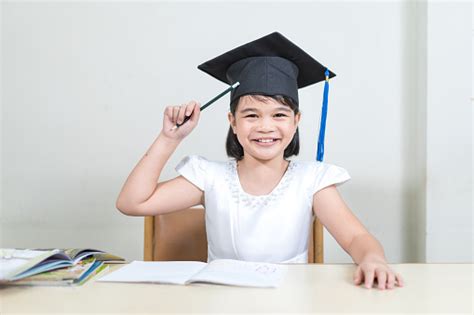 쾌활한 아시아 의 어린 소녀 학생의 초상화는 박격포 또는 졸업 모자를 착용하고 연필을 잡고 복사 공간이있는 흰색 배경이있는 노트북에 씁니다 교육 졸업 개념 스톡 사진 개념에