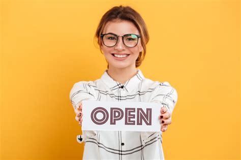 열린 표지판을 들고 카메라를 보고 노란 배경위에 고립된 격자 무늬 셔츠를 입은 웃는 여성의 초상화 갈색에 대한 스톡 사진 및 기타 이미지 Istock