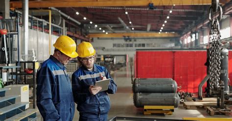 작업복을 입은 두 명의 남성 엔지니어가 대형 작업장이나 공장 한가운데에 서서 새로운 산업 장비의 특성에 대해 논의하고 있다 사진 Unsplash의 능률 이미지
