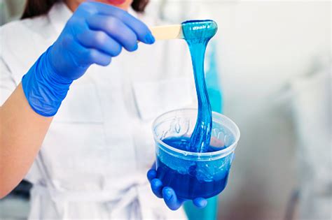 흰색 코트를 입은 소녀 미용사는 미용실에서 주걱으로 편집할 수 있는 푸른 설탕 페이스트를 들고 있습니다 주걱 과 제모 페이스트를 손에 넣습니다 슈가링 건강관리와 의술에 대한