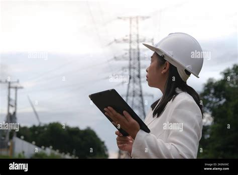 Asian Female Electrical Engineer Working On Tablet Near High Voltage Pole Inspecting Power Grid