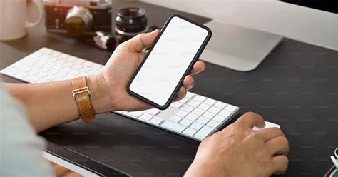 데스크탑 컴퓨터로 작업하는 동안 빈 화면 휴대폰을 들고 있는 창의적인 세련된 손 사진 Unsplash의 사진술 이미지