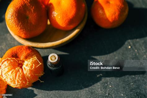 껍질을 벗긴 오렌지와 나무 그릇에 담긴 신선한 귤 옆에 놓인 에센셜 오일이 담긴 호박색 유리병의 클로즈업 이미지는 따뜻하고 소박한 배경으로 천연 시트러스 아로마테라피를