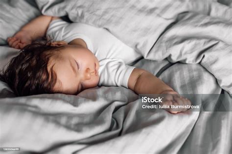 집에서 침대에 회색 담요 아래에 누워 잠옷에 예쁜 아기의 초상화 침실에서 잠자는 유아 아이는 달콤한 꿈을 참조하십시오 회색 배경 무료 복사 공간 육아 및 건강한 수면 개념