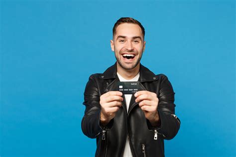 검은 가죽 자 켓 흰색 T 셔츠에 잘생긴 세련 된 젊은 면은 남자 파란색 벽 배경 스튜디오 초상화에 고립 된 손에 신용 카드를 개최 합니다 사람들 라이프 스타일 개념입니다