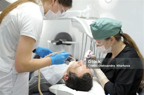 치아 뽑기 치과에서 치아 뽑기 중년 두 명의 여성 간호사와 의사가 치과 진료실에서 환자를 구부리고 검은색 보조 수술용 장갑을