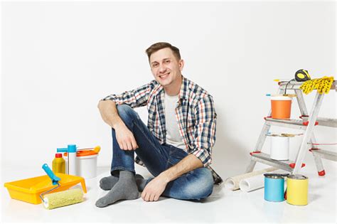 캐주얼 옷 흰색 배경에 고립 된 재건축 아파트 룸에 대 한 악기와 함께 바닥에 앉아에서 웃는 행복 한 남자 벽지 액세서리를 붙이기 그림 도구 수리 가정 개념입니다 개선에