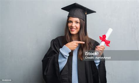 손과 손가락으로 가리키는 매우 행복도 들고 대학원 제복을 입고 그런 지 회색 벽에 젊은 갈색 머리 여자 가리키기에 대한 스톡 사진 및 기타 이미지 Istock