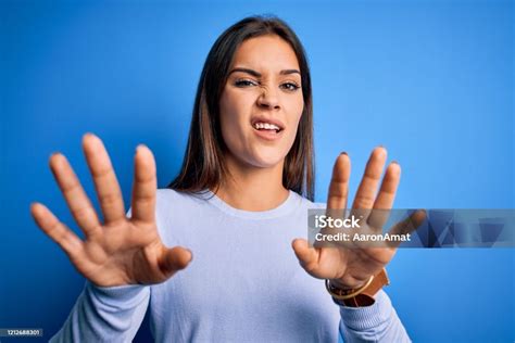 젊은 아름 다운 갈색 머리 여자 캐주얼 스웨터를 입고 파란색 배경 에 서 두려워 하 고 두려움 표정 중지 제스처 손으로 충격에 외치고 공황 개념 갈색 머리에 대한 스톡 사진