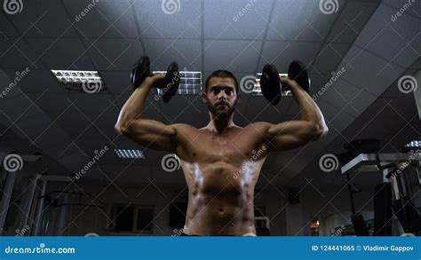Muscular Man In The Gym Training With Dumbbells Guy Pumps His Deltoid