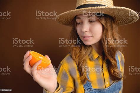 밀짚 모자와 작업복을 입은 젊은 백인 여성이 손에 오렌지색 반을 들고 그녀를 바라 봅니다 스튜디오 초상화 20 29세에 대한