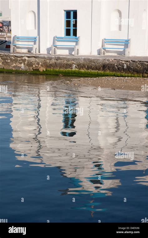 Benches Outside The Blue And White Agios Nikolaos Church On The Waterfront And Reflection In