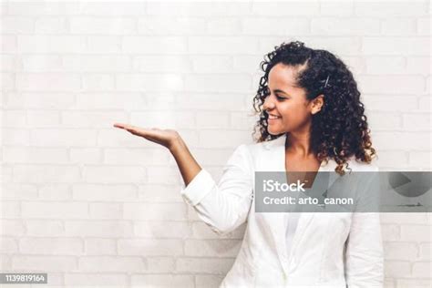 웃는 아름 다운 직업적인 사업 아프리카계 미국인 까만 여자 백색 벽돌 벽 배경 가까이에 서 있는 열려있는 손에 빈 복사 공간을 보여주는 광고에 대한 스톡 사진 및 기타
