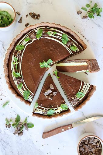 슬라이스 민트 초콜릿 타르트 바삭바삭하고 플루티드 코코아 페이스트리 크러스트 화이트 초콜릿 초콜릿 조각 그릇 민트 잎 잔가지 칼 부스러기 대리석 효과 배경 높은 전망 0명에