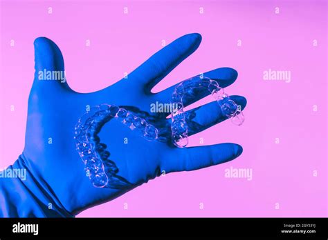 A Hand In A Blue Glove Holds Aligners For Aligning Teeth On A Pink Background Plastic Braces