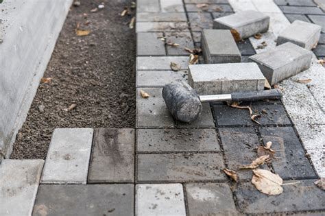 그의 오렌지에 작성기의 손에 새로운 외관 포장 돌 신중 하 게 배치 위치에 수평 하 게 하 고 레이크 토양에 기본 피팅 망치로 손을 Gloved 모래 기초입니다 건물입니다