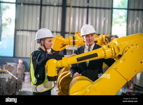 An Engineer And An Executive Collaborate In A Robotics Factory Examining A Robotic Arm Closely