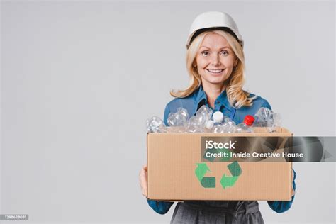 회색 배경에 고립 된 재활용을위해 플라스틱 병으로 가득 찬 상자를 들고 단단한 모자를 쓴 쾌활한 중년 백인 여성 미소에 대한 스톡 사진 및 기타 이미지 Istock